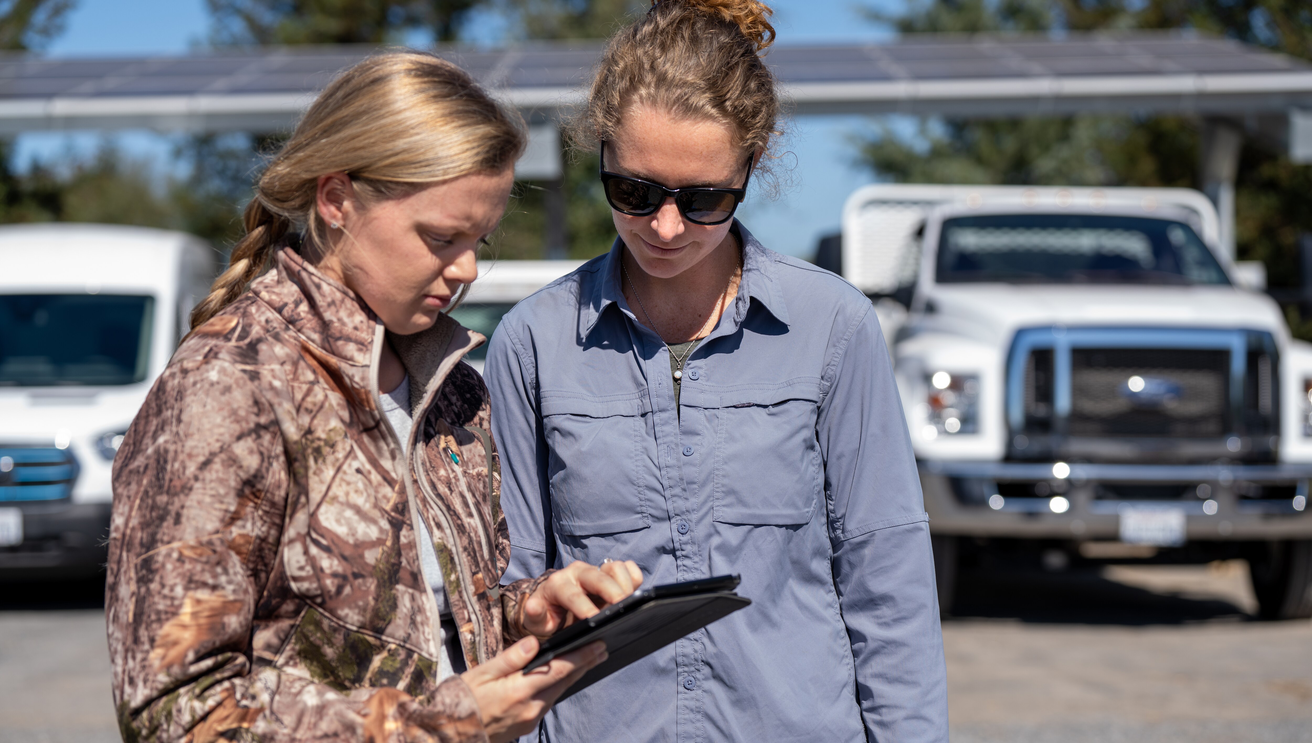 Two people looking at a tablet with a Ford fleet vehicles in background